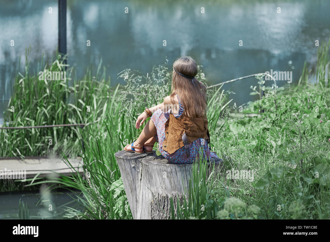 beautiful hippie girl sitting on a stump and looking at the pond. the concept of unity with ...