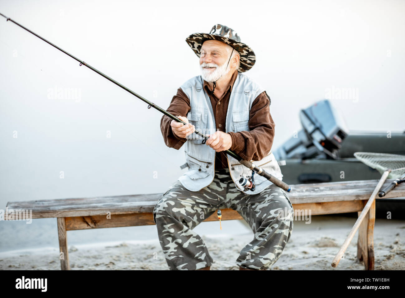 Cheerful senior man preparing for the fishing while sitting on the ...