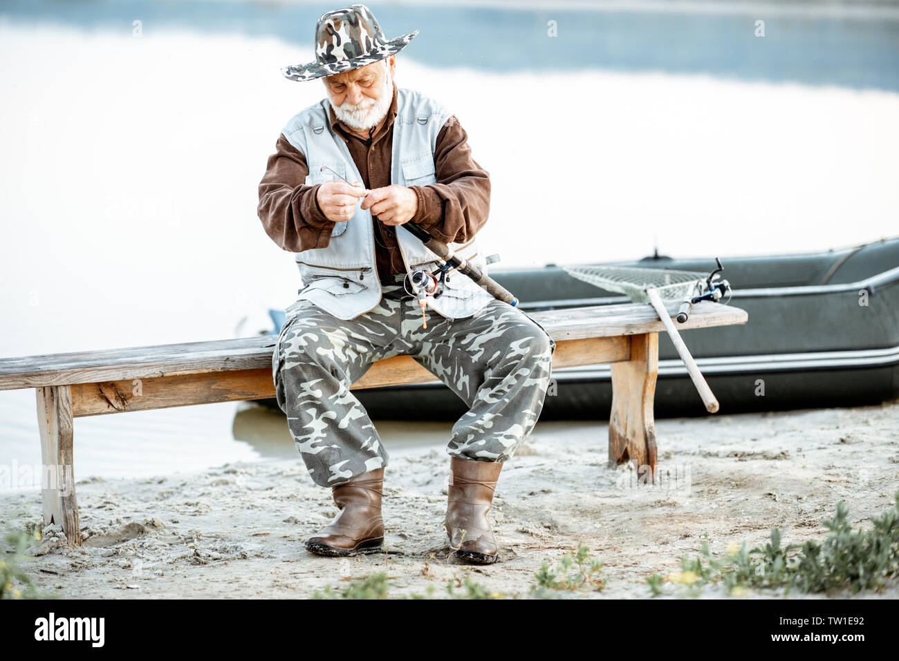 Cheerful senior man preparing for the fishing while sitting on the ...