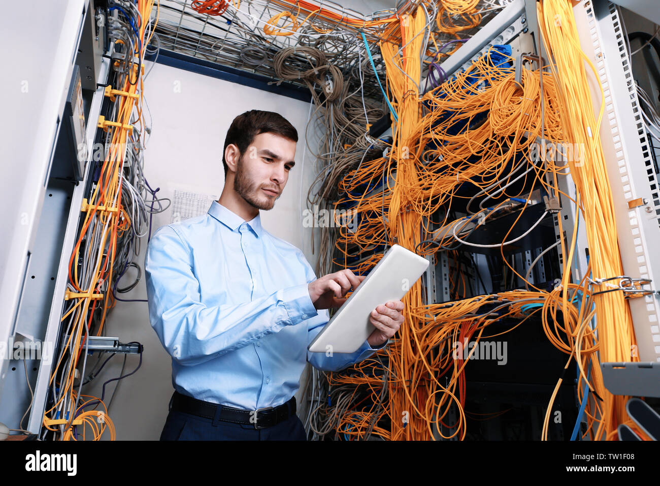 Handsome young engineer with tablet computer working in server room ...