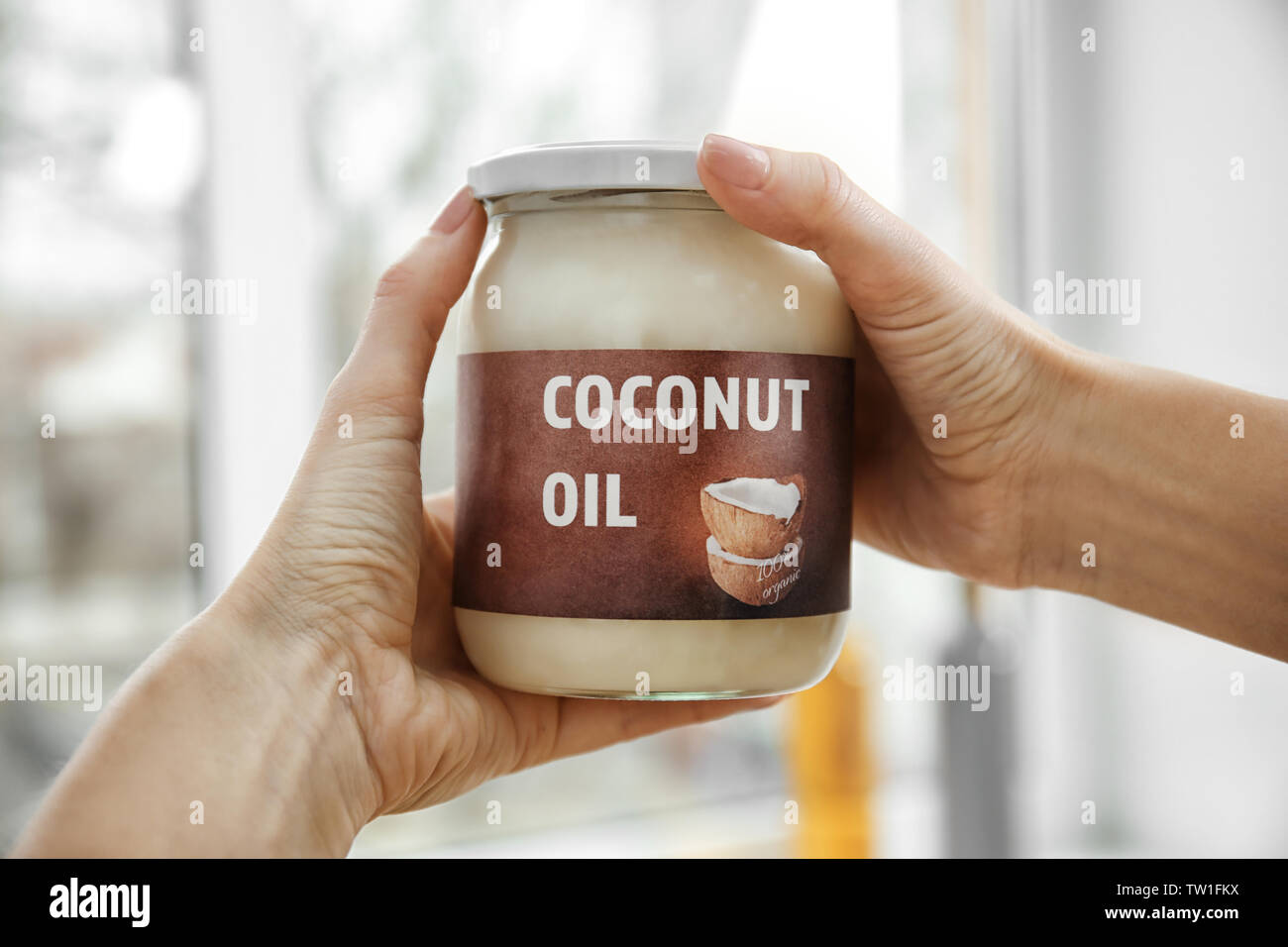 Female hands holding jar with coconut oil on blurred background Stock ...
