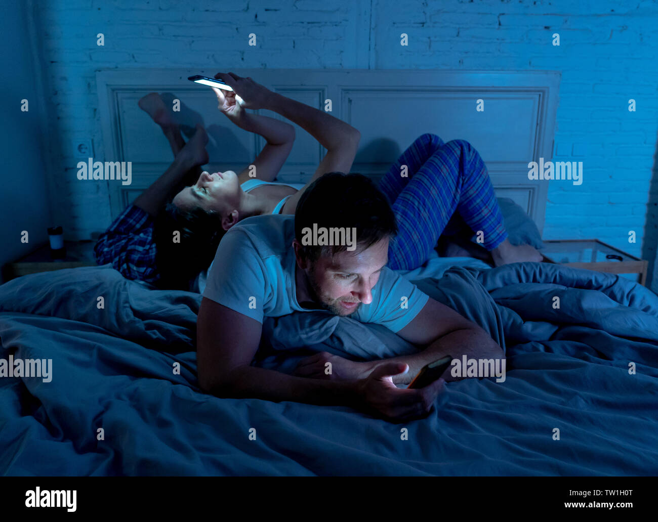 Sad man and woman married couple using their smart mobile phone in bed ...