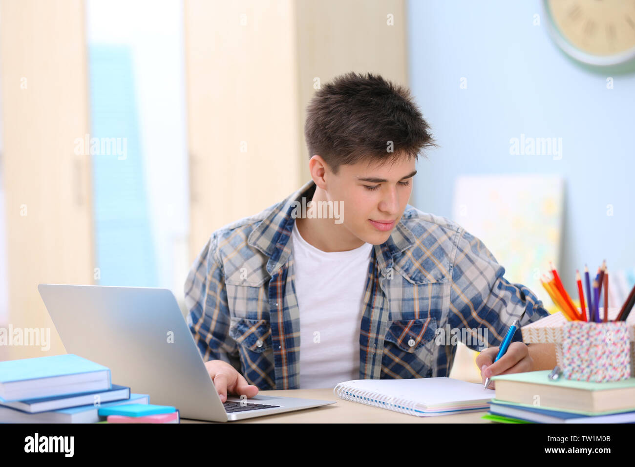 Teenager using laptop and taking notes at home Stock Photo - Alamy
