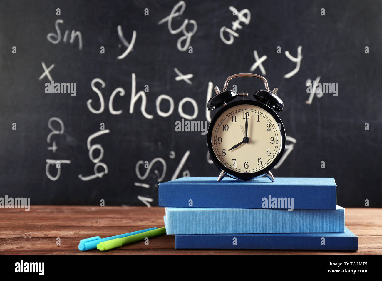 Books and alarm clock on blackboard background Stock Photo - Alamy
