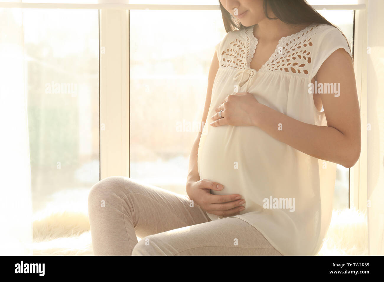 Beautiful pregnant woman sitting on window sill at home Stock Photo - Alamy
