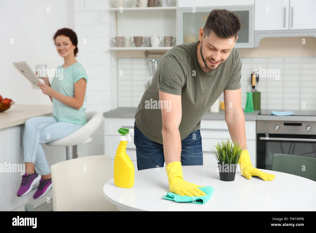 Woman reading newspaper and drinking coffee while man cleaning kitchen ...