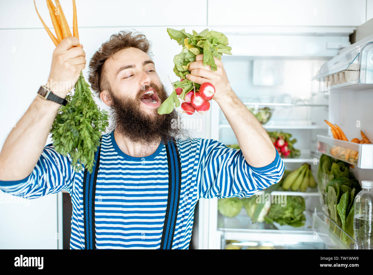 Portrait of a well-looking man with carrot and radish in front of the ...