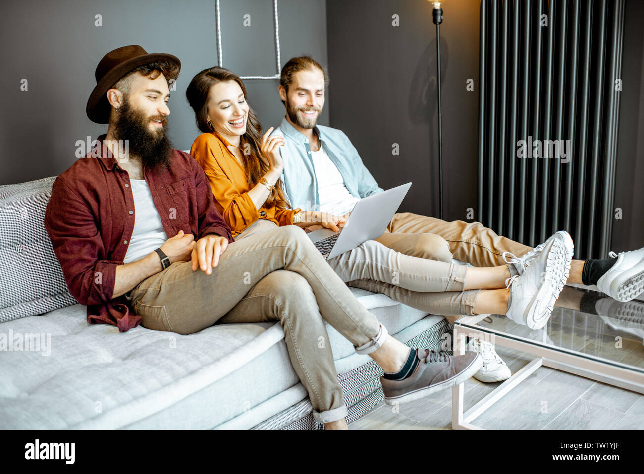 Young friends having fun sitting together on the couch with laptop in ...