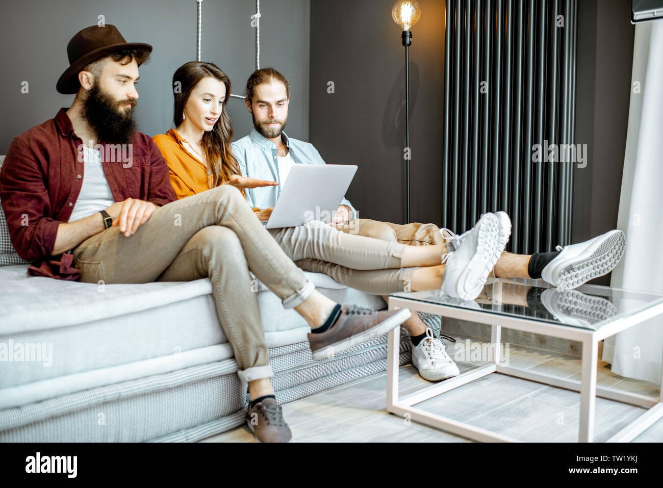 Young friends having fun sitting together on the couch with laptop in ...