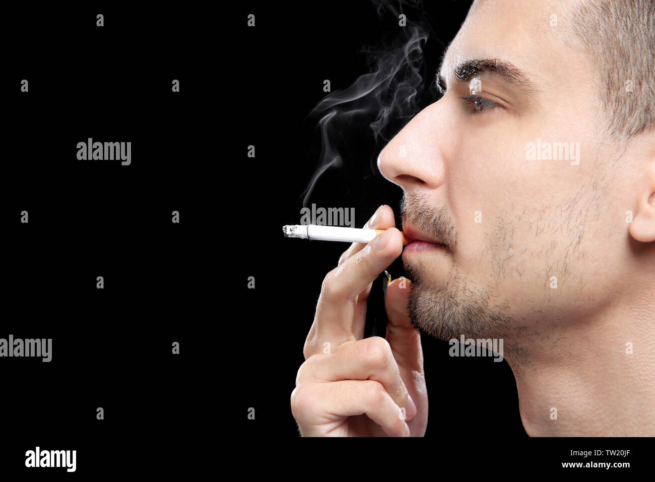 Young man smoking cigarette on black background Stock Photo - Alamy