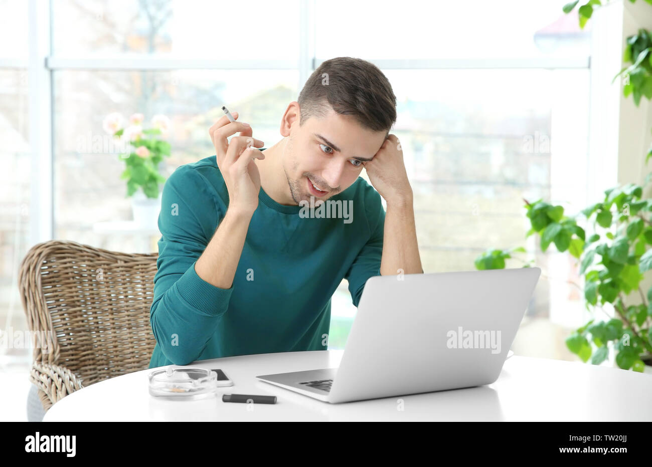 Young man using laptop and smoking cigarette Stock Photo - Alamy