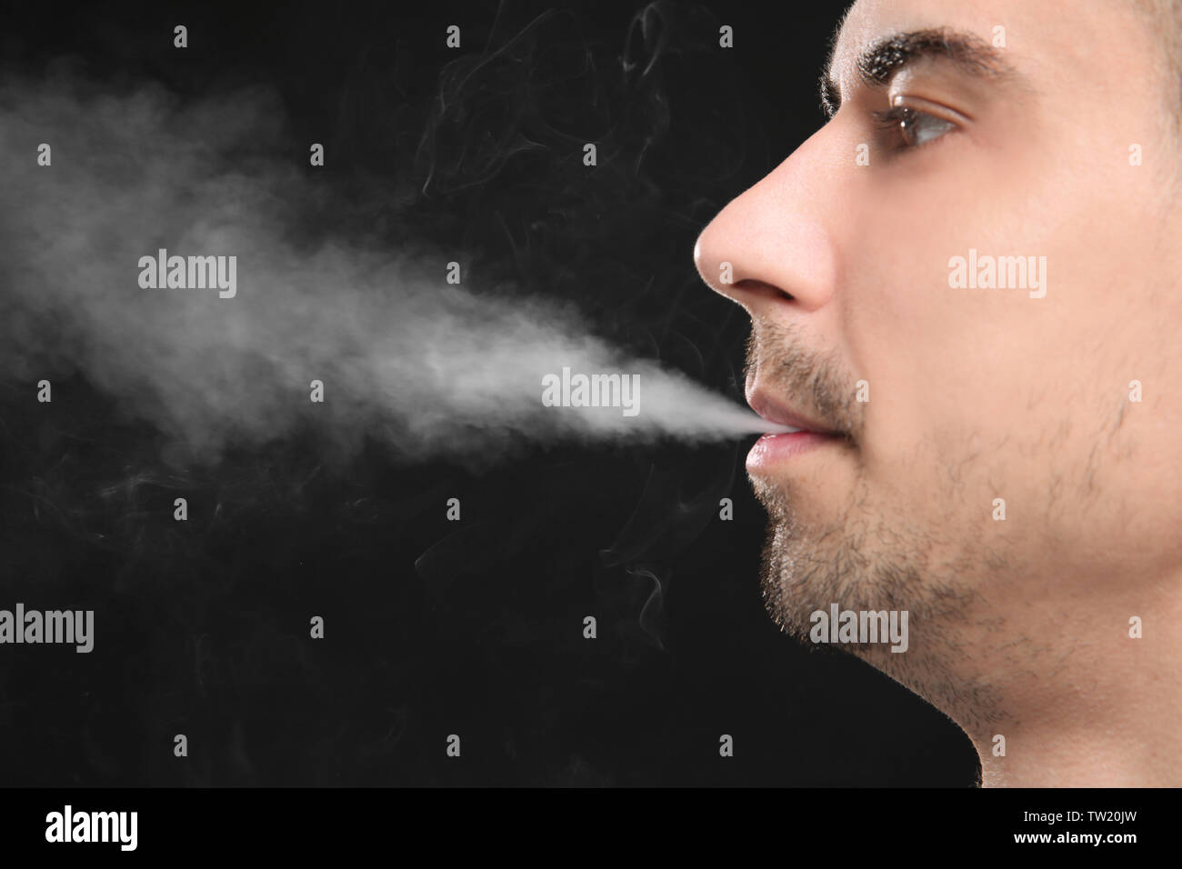 Young man exhaling smoke on black background Stock Photo - Alamy