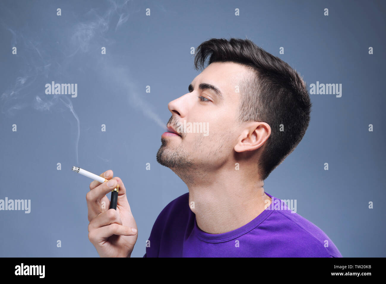 Young man smoking cigarette on color background Stock Photo - Alamy