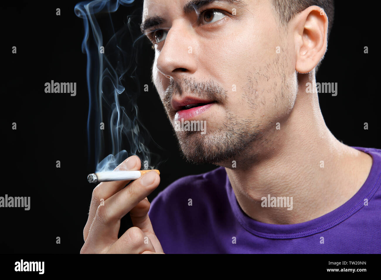 Young man smoking cigarette on black background Stock Photo - Alamy