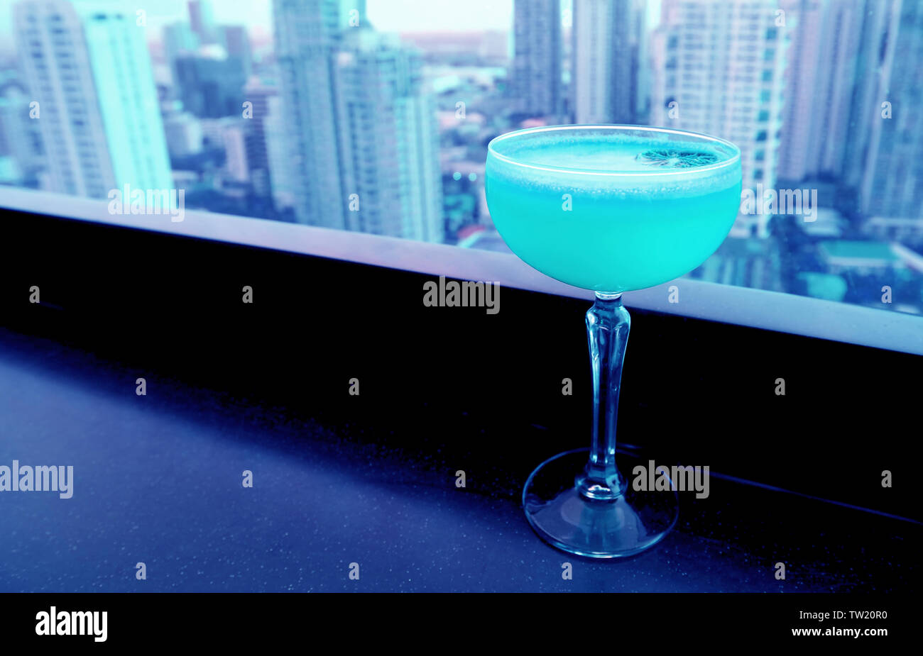 Aqua blue colored cocktail on the rooftop bar's table with skyscrapers ...