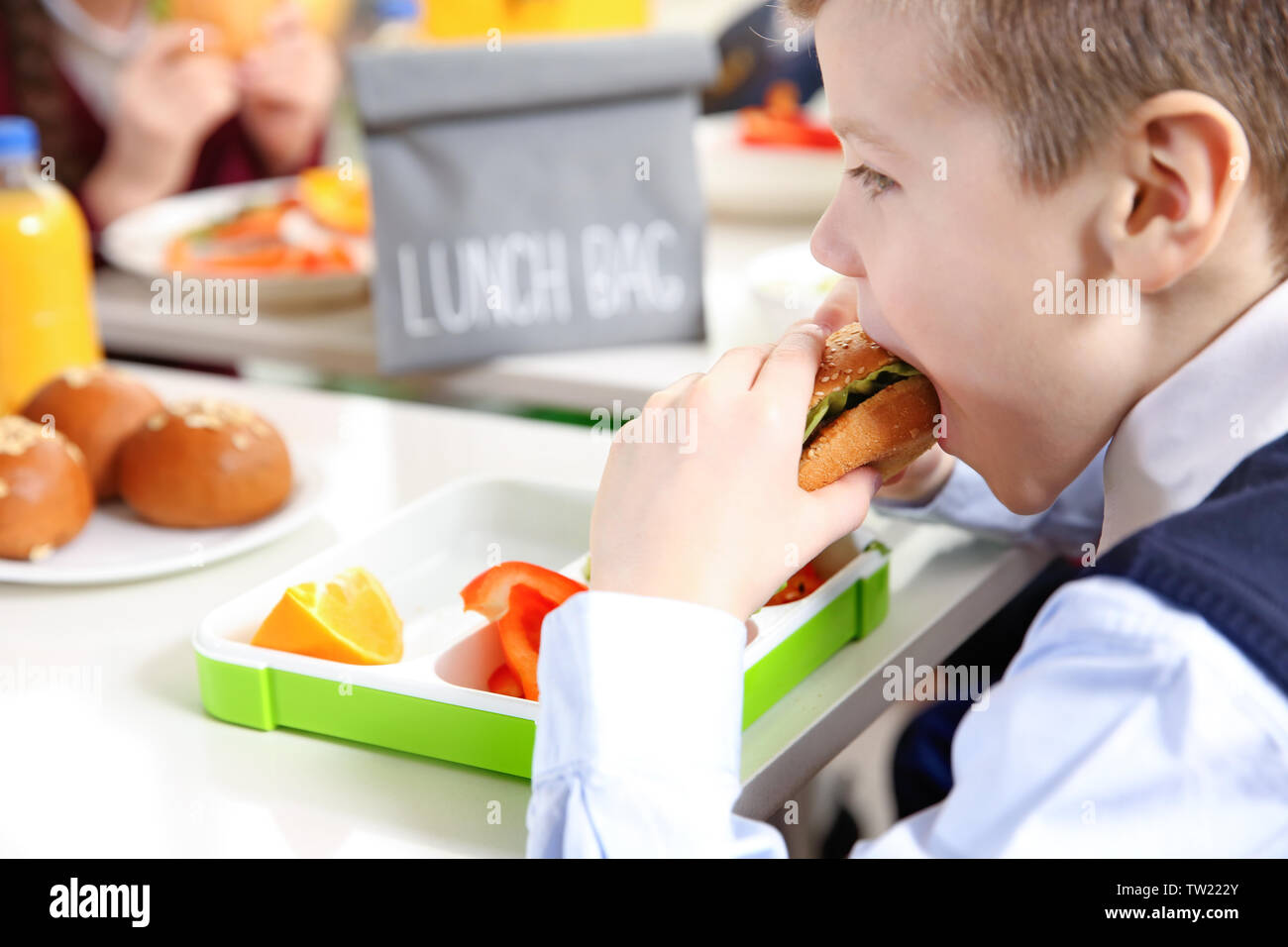 School boy eating sandwich while sitting at table in school cafeteria ...