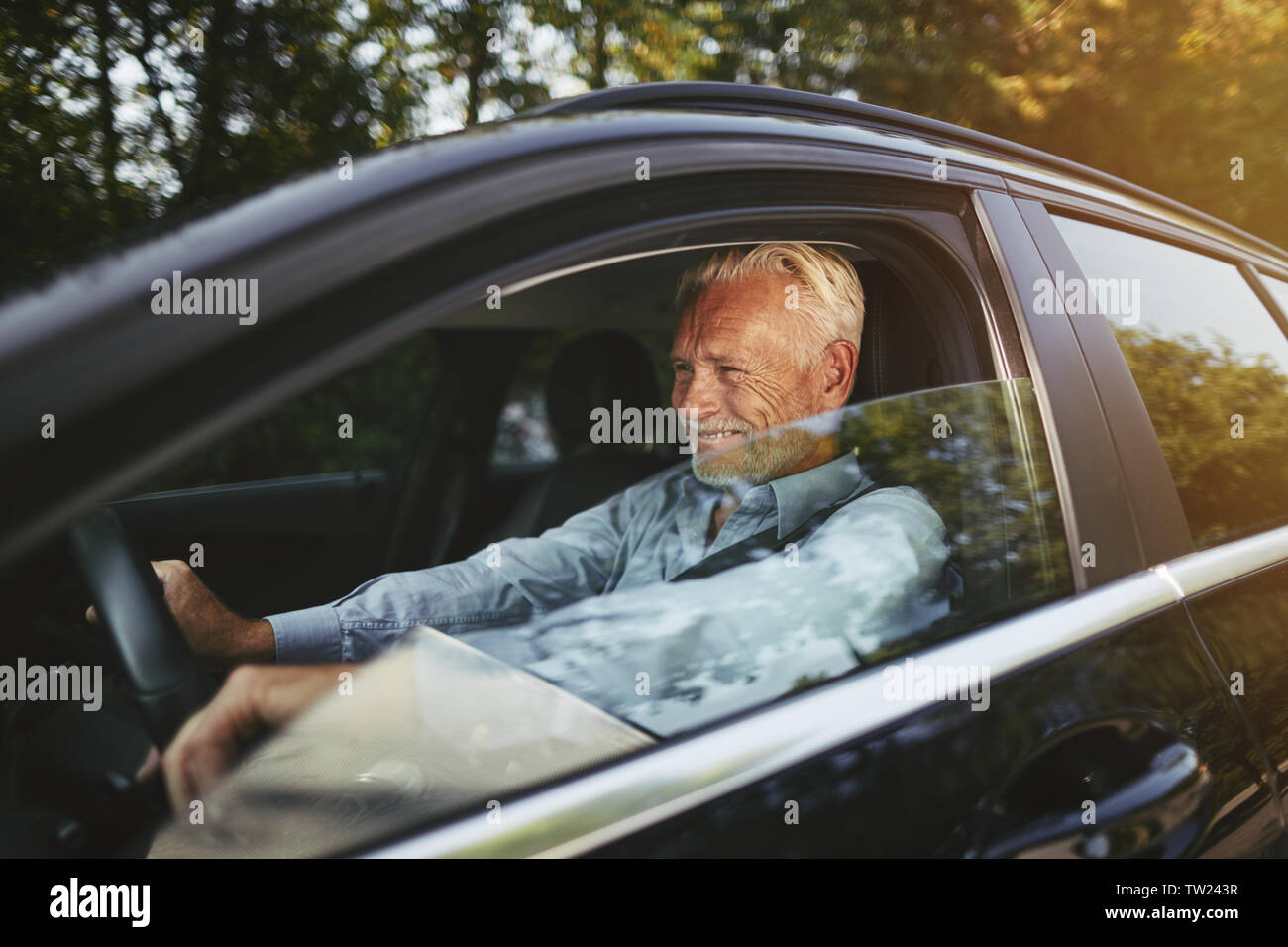 Senior man smiling while sitting alone in his car enjoying a drive on a ...