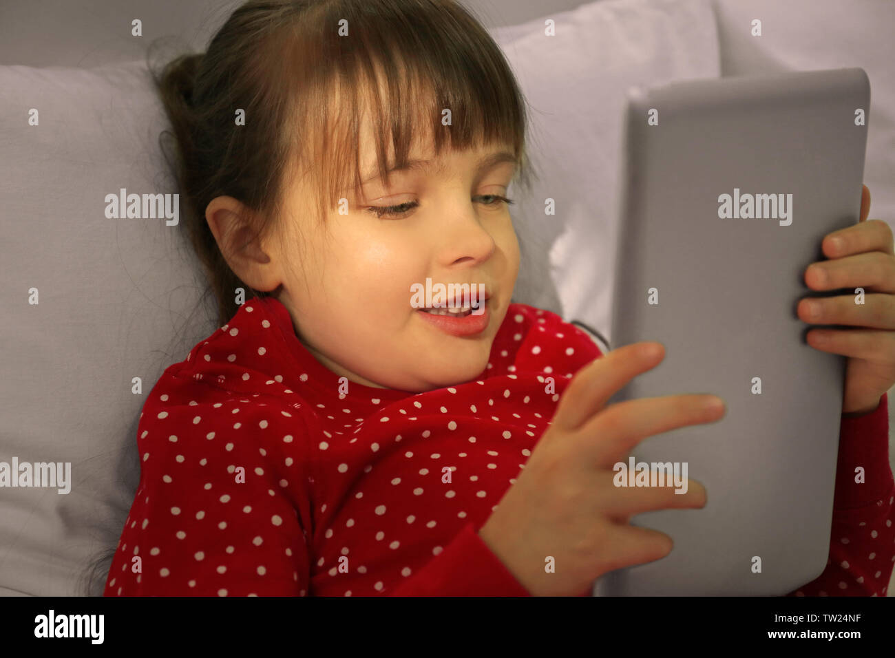 Cute little girl playing with tablet on white bed Stock Photo - Alamy