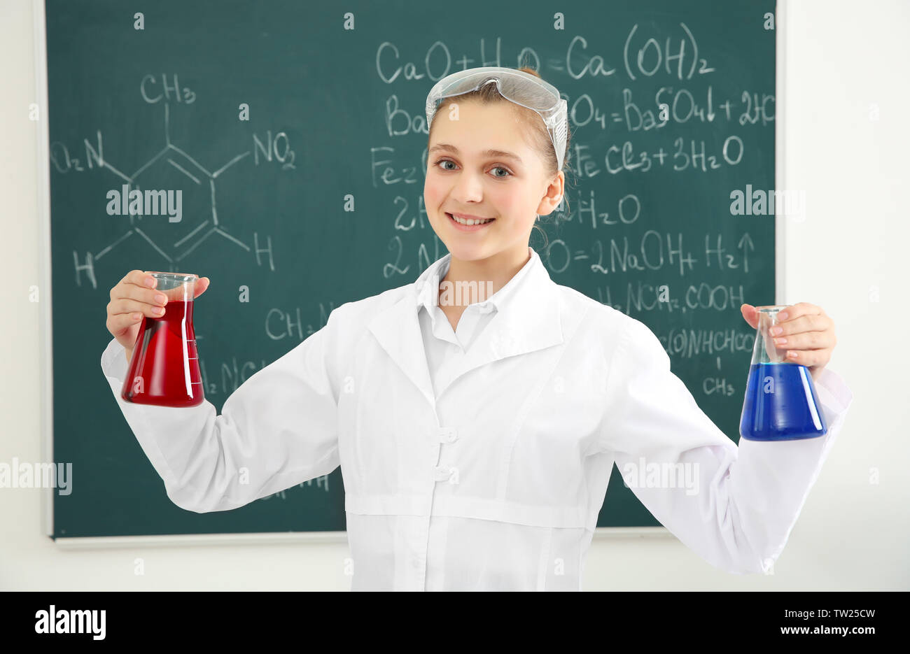 Beautiful school girl holding flasks near chalkboard in chemistry class ...