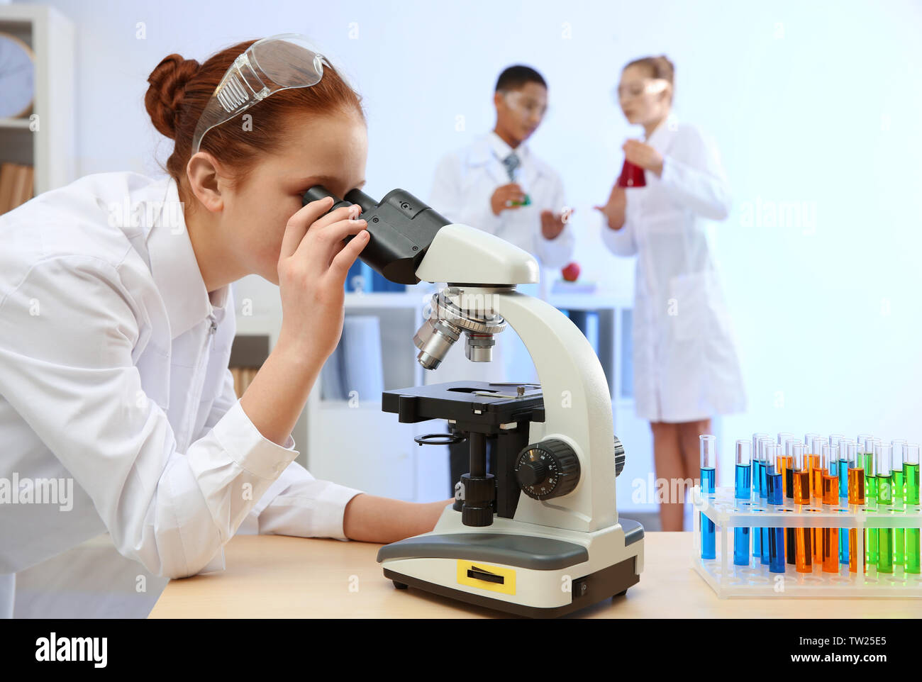 Beautiful school girl looking through microscope in chemistry class ...