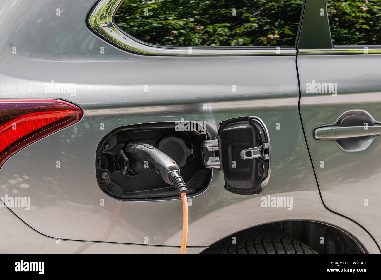 A passenger car is electrically charged via a plug and cord connected ...