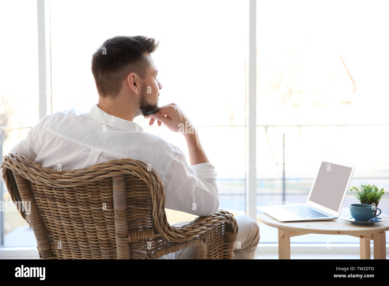 Happy young man resting in wicker chair near big window Stock Photo - Alamy