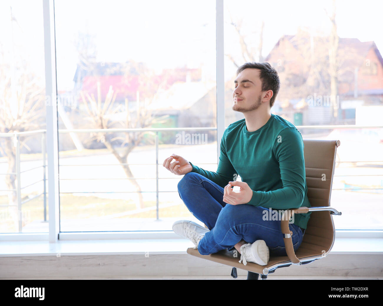 Happy young man sitting on chair and meditating Stock Photo - Alamy