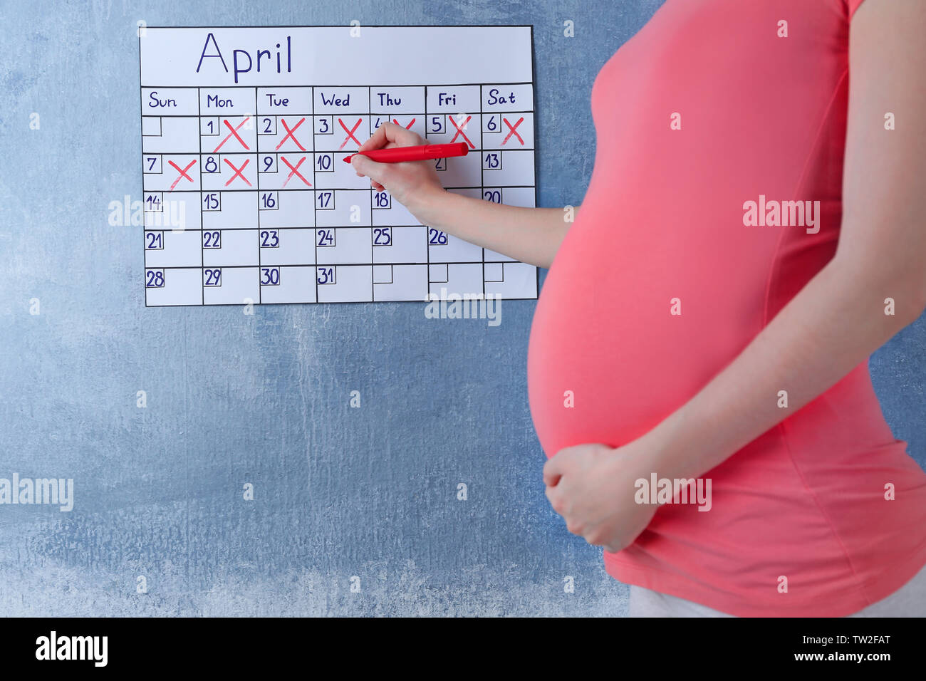 Young pregnant woman counting days with calendar to baby birth on color ...