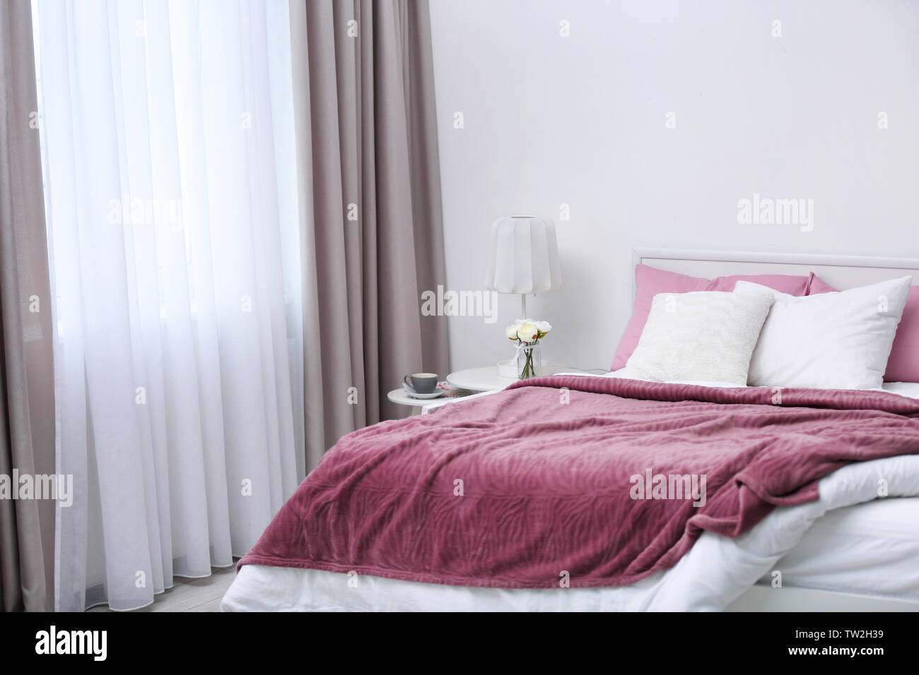 Comfortable bed with soft pink coverlet and pillows in light modern ...