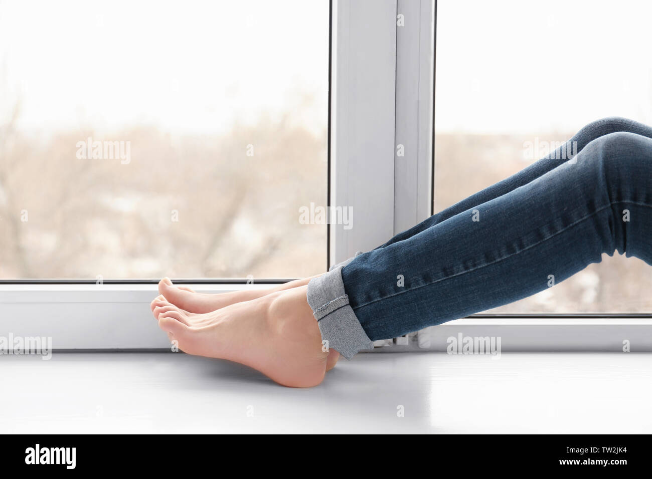 Legs of young woman sitting on window sill at home Stock Photo - Alamy