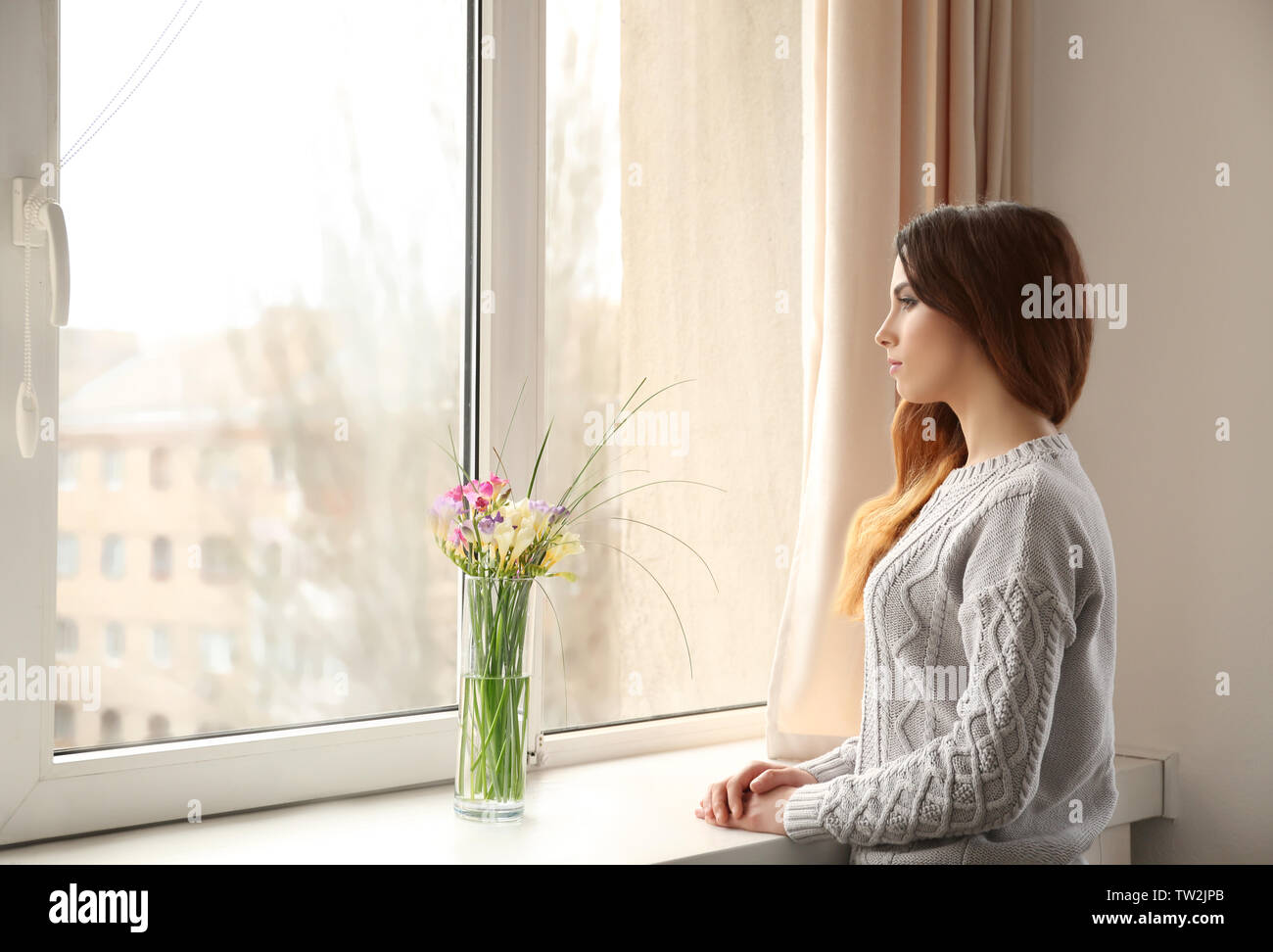 Beautiful young woman with bouquet of flowers near window at home Stock ...