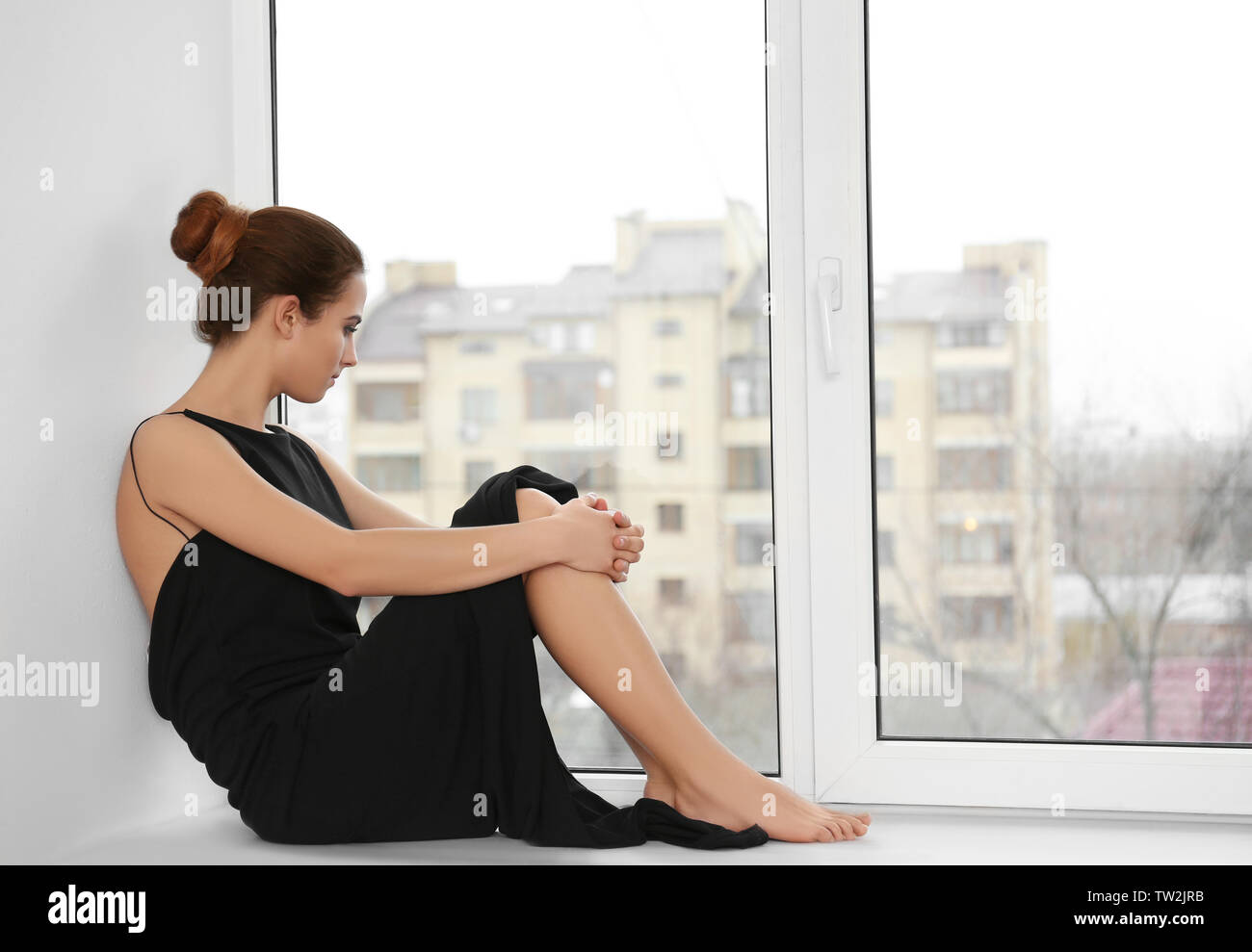 Beautiful young woman sitting on window sill at home Stock Photo - Alamy