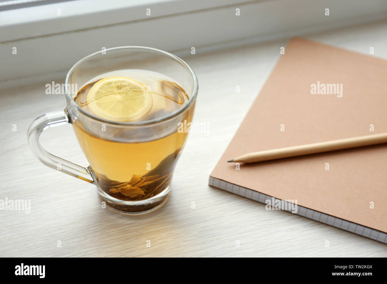Cup of hot tea, notebook and pencil on window sill Stock Photo - Alamy
