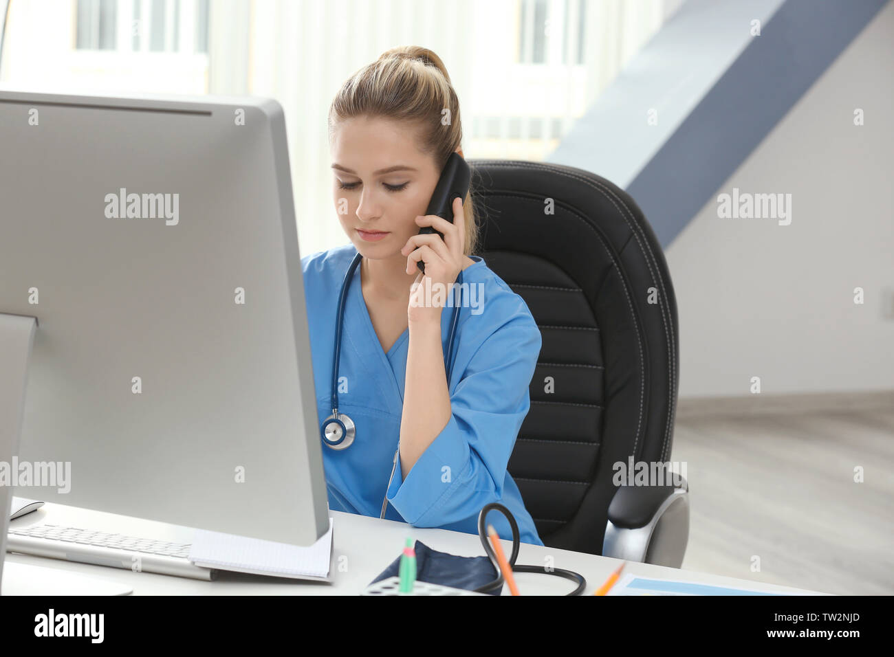 Young medical assistant talking by telephone while working in office ...
