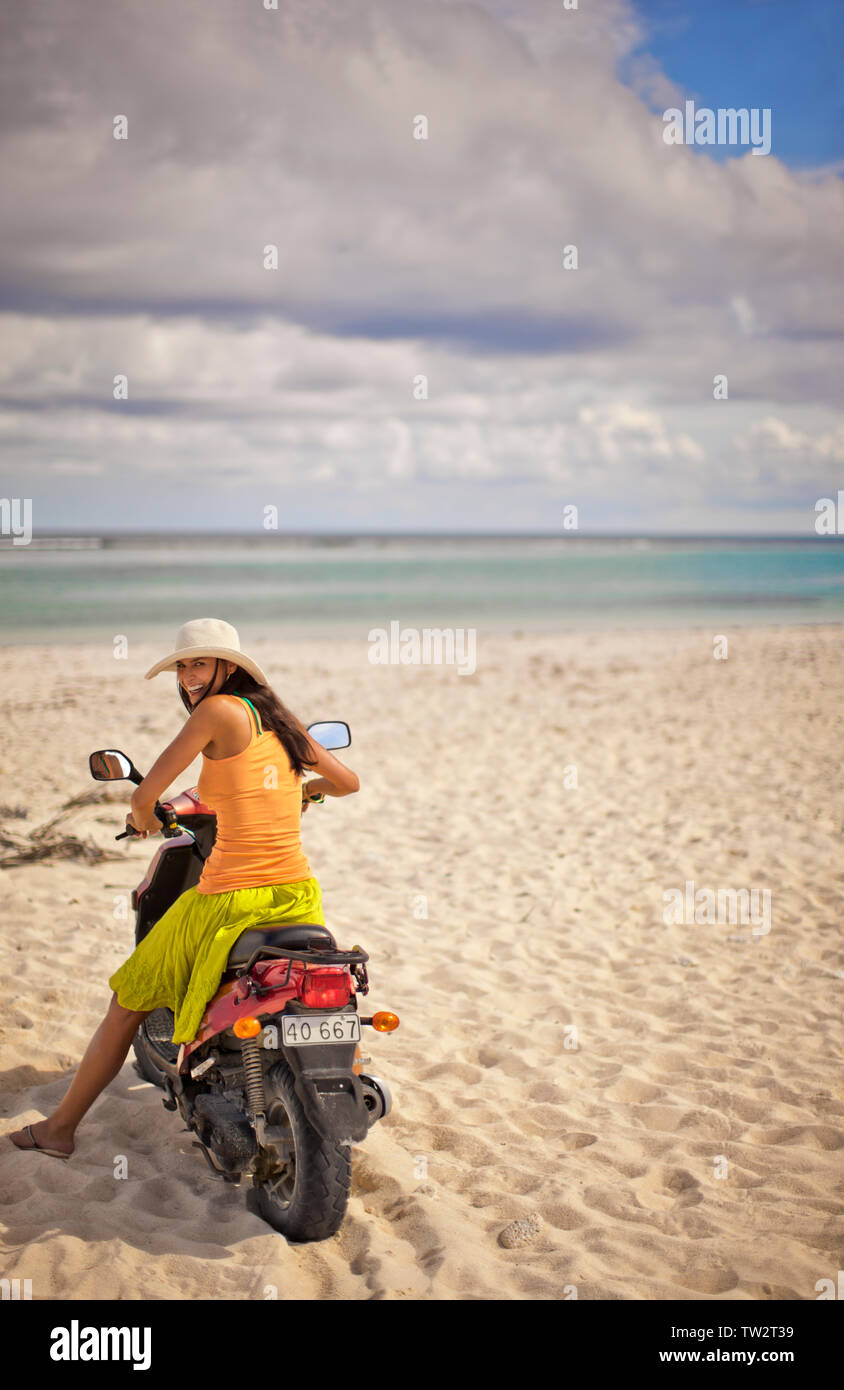 Smiling young woman having fun on a moped scooter at a tropical beach ...