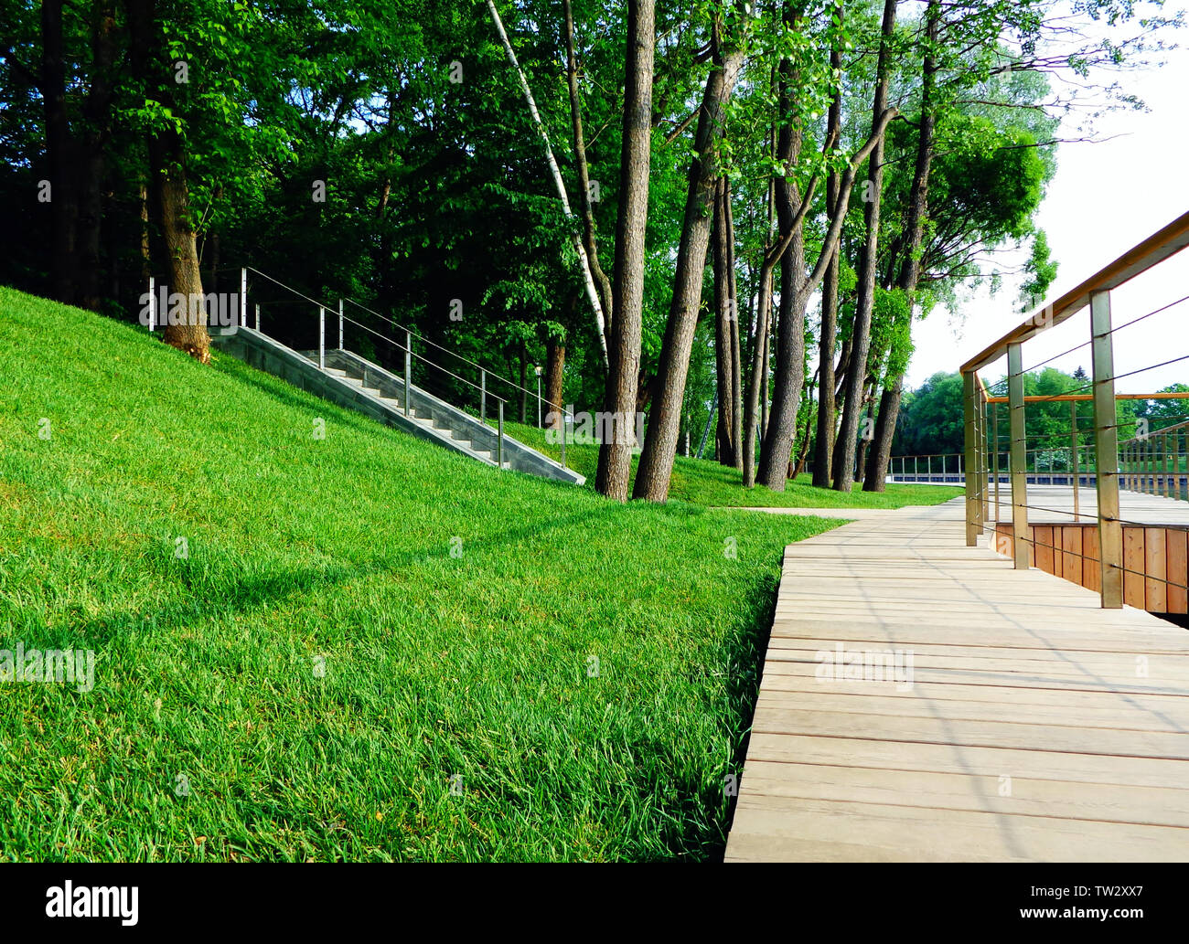 Wooden walking path with railings along the pond in well groomed park ...