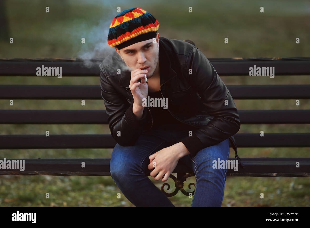 Young man smoking weed while sitting on bench outdoors Stock Photo - Alamy