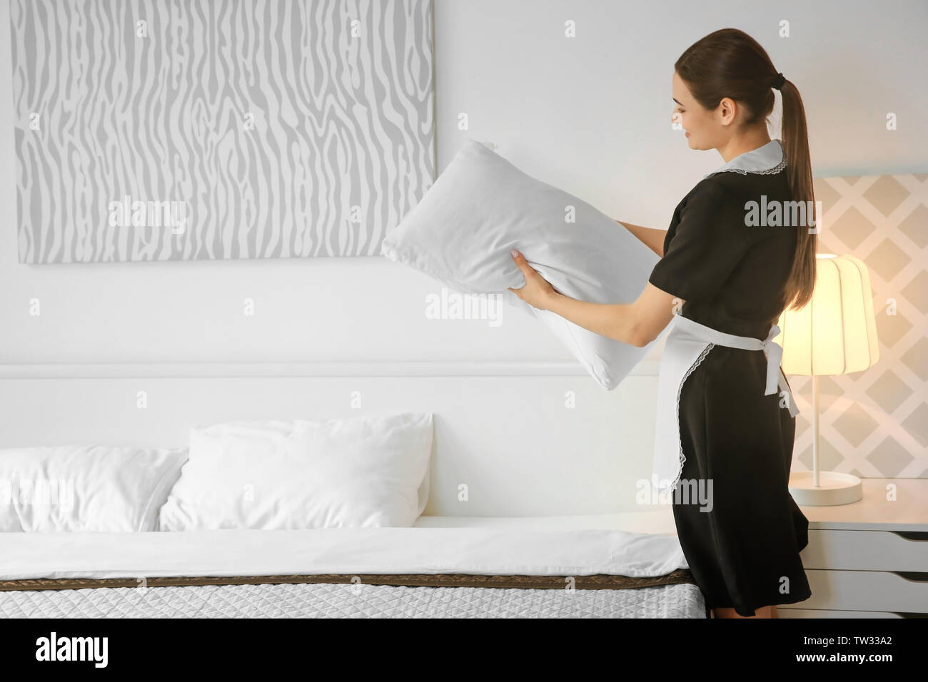 Young maid making bed in light hotel room Stock Photo - Alamy