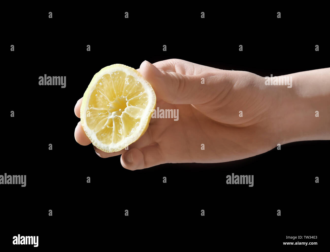 Female hand holding half of lemon on black background Stock Photo - Alamy
