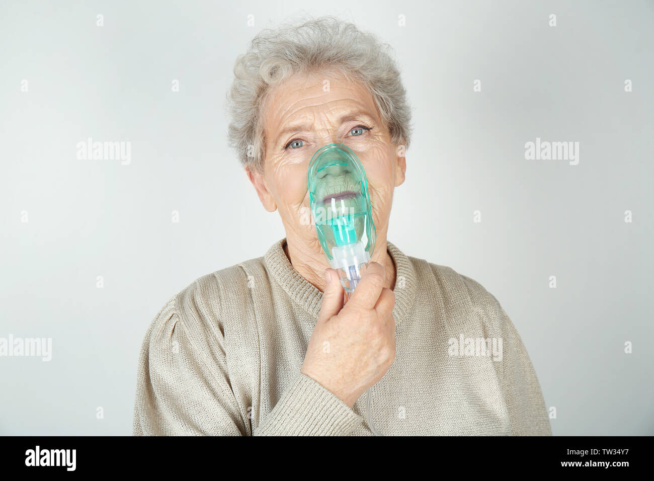 Elderly woman using asthma machine on light background Stock Photo - Alamy