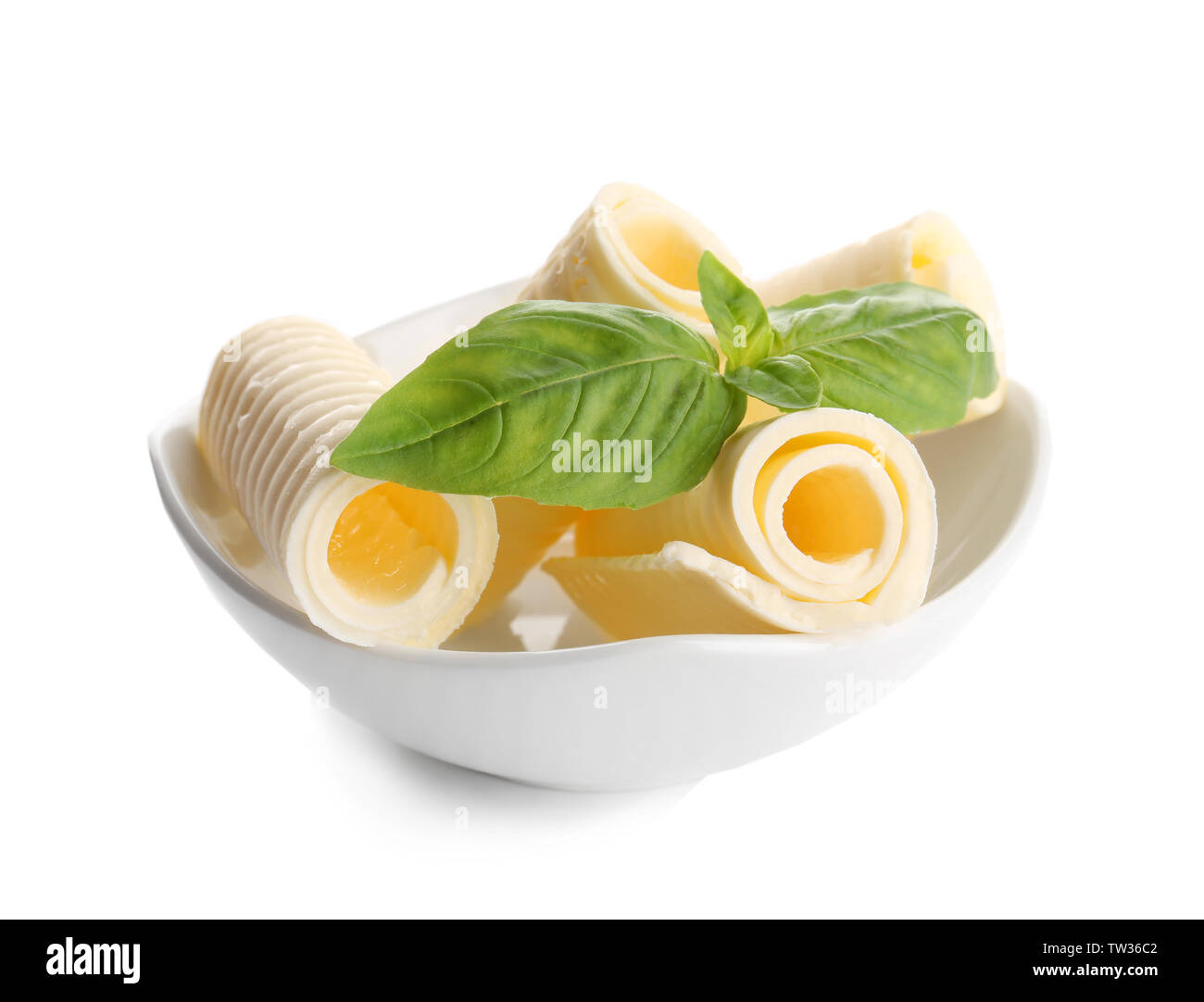 Delicious butter curls with basil leaves in bowl on white background ...