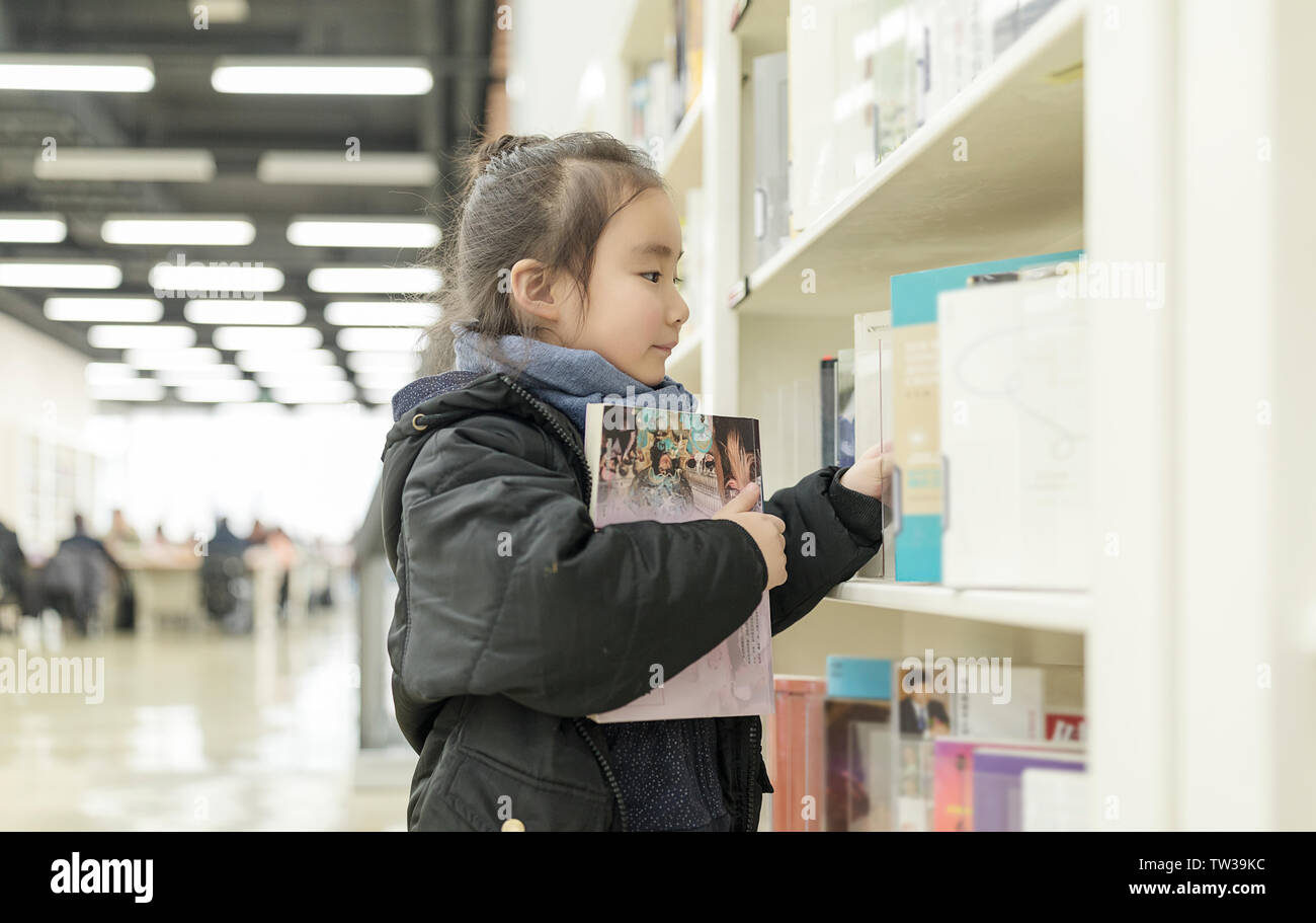 Little Asian girl reading in the library Stock Photo - Alamy