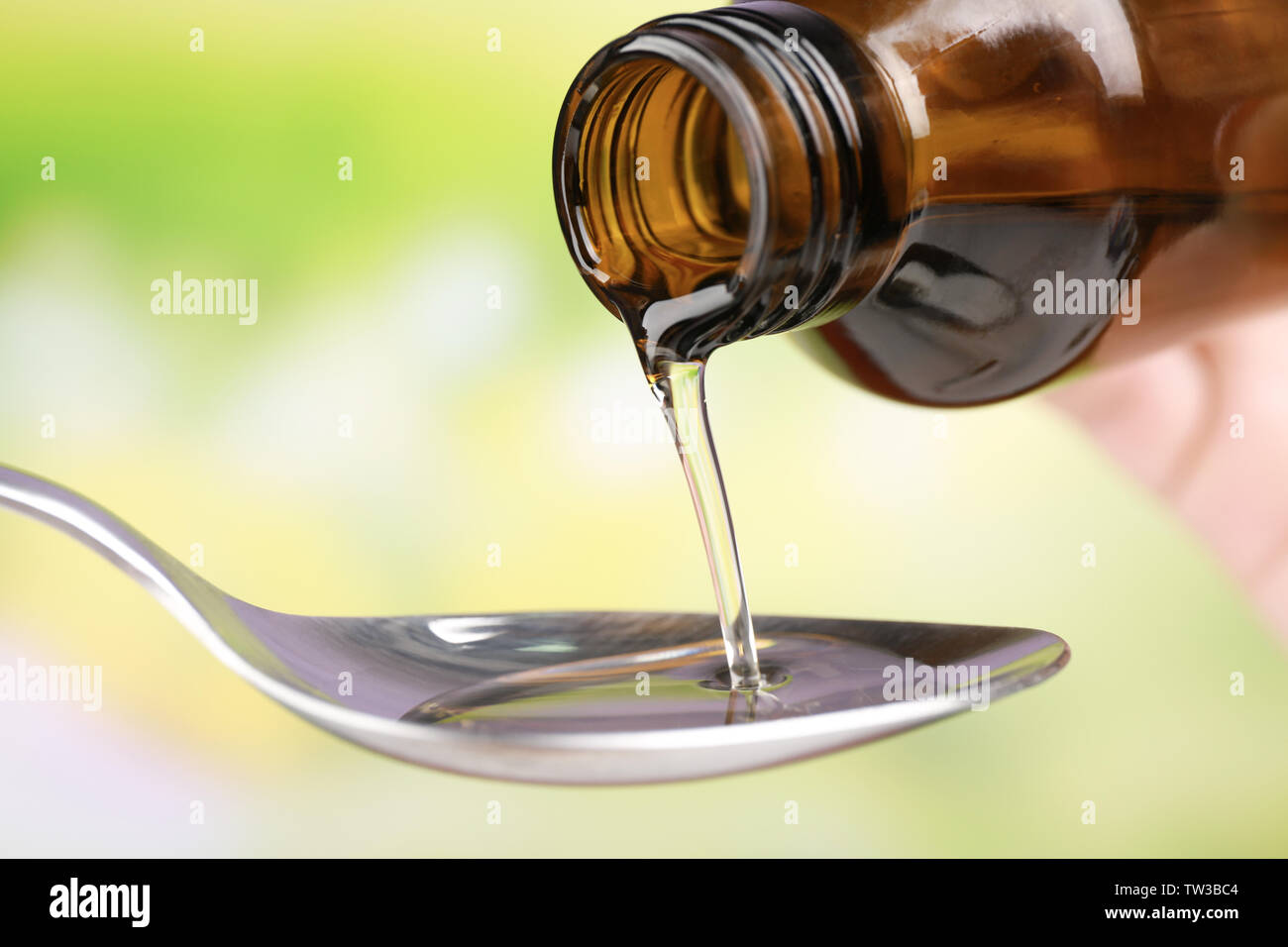 Pouring cough syrup into spoon on blurred background Stock Photo - Alamy