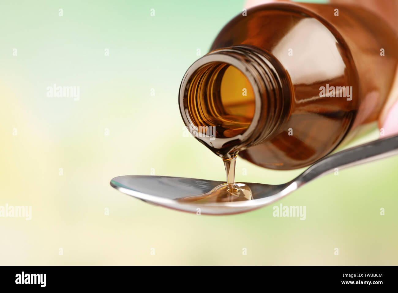Pouring cough syrup into spoon on blurred background Stock Photo - Alamy