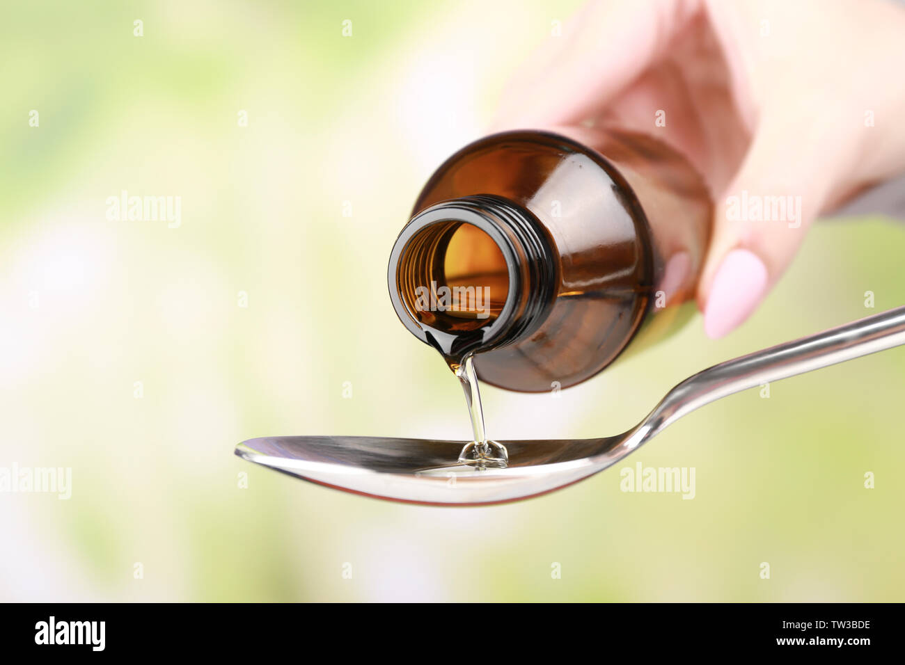 Pouring cough syrup into spoon on blurred background Stock Photo - Alamy
