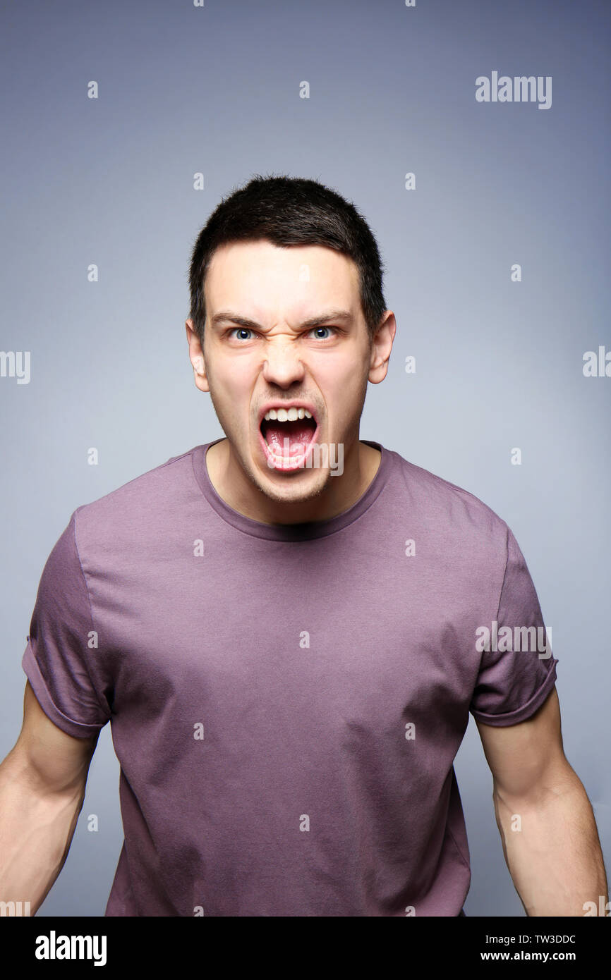 Handsome angry young man on gray background Stock Photo - Alamy