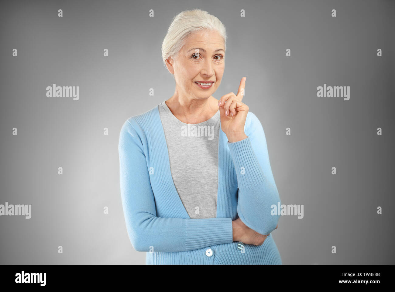 Beautiful elegant elderly woman pointing with finger on gray background ...