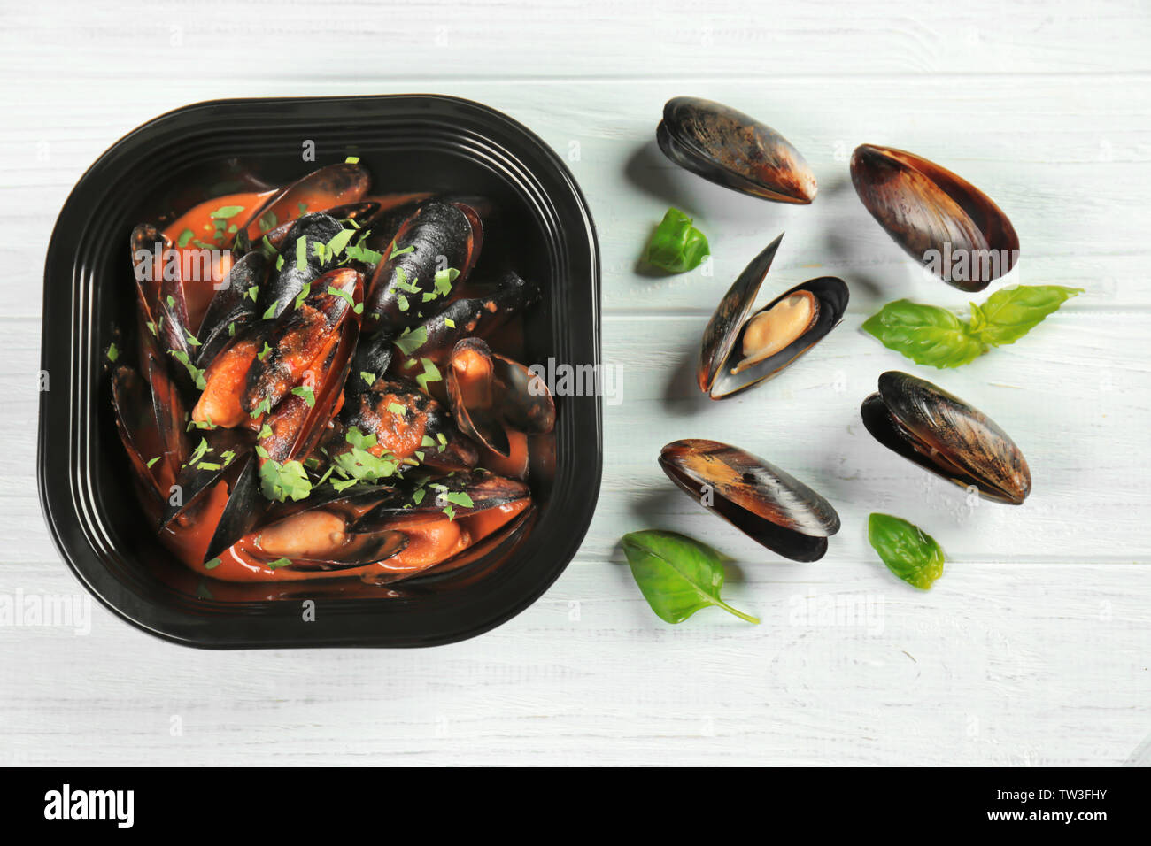 Plastic container with delicious mussels in tomato sauce on wooden ...