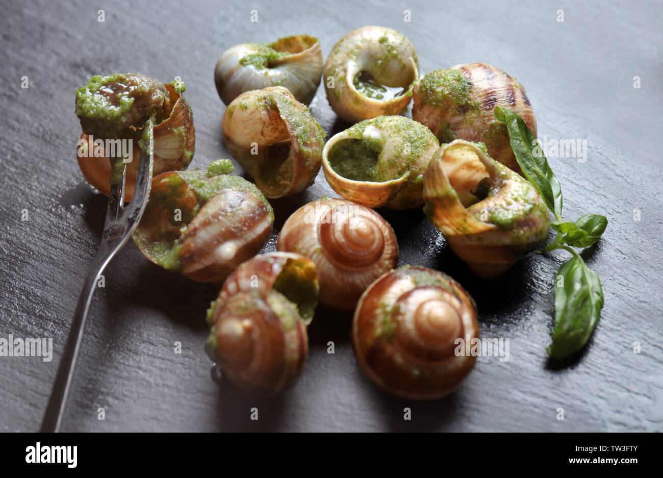 Delicious snails in green sauce and fork on dark table Stock Photo - Alamy
