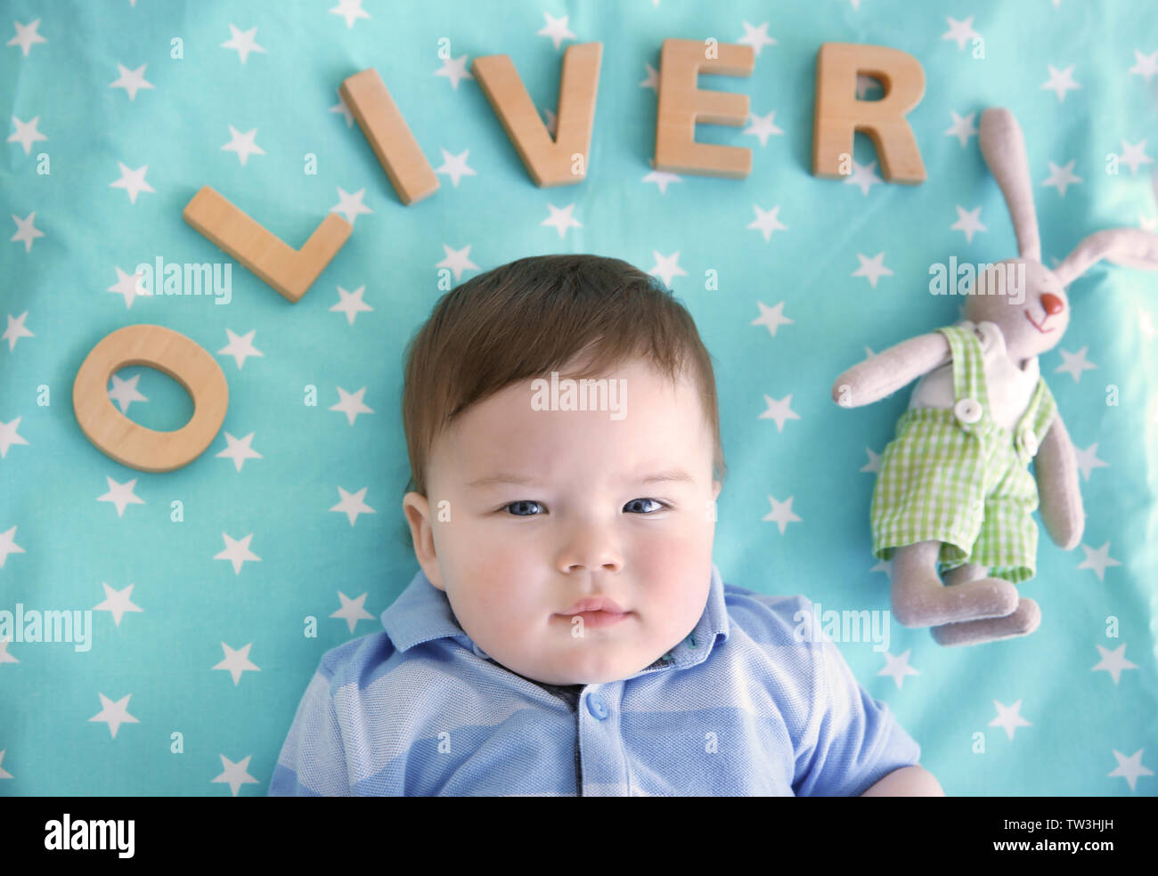 Cute baby lying on bed with word OLIVER composed of wooden letters ...